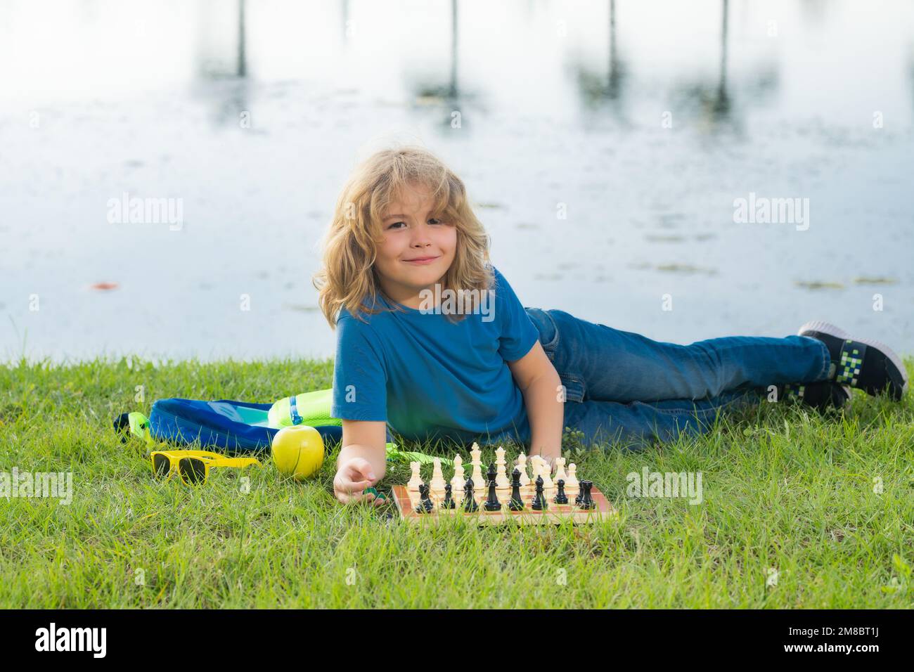 Child playing chess game in spring backyard, laying on grass ...