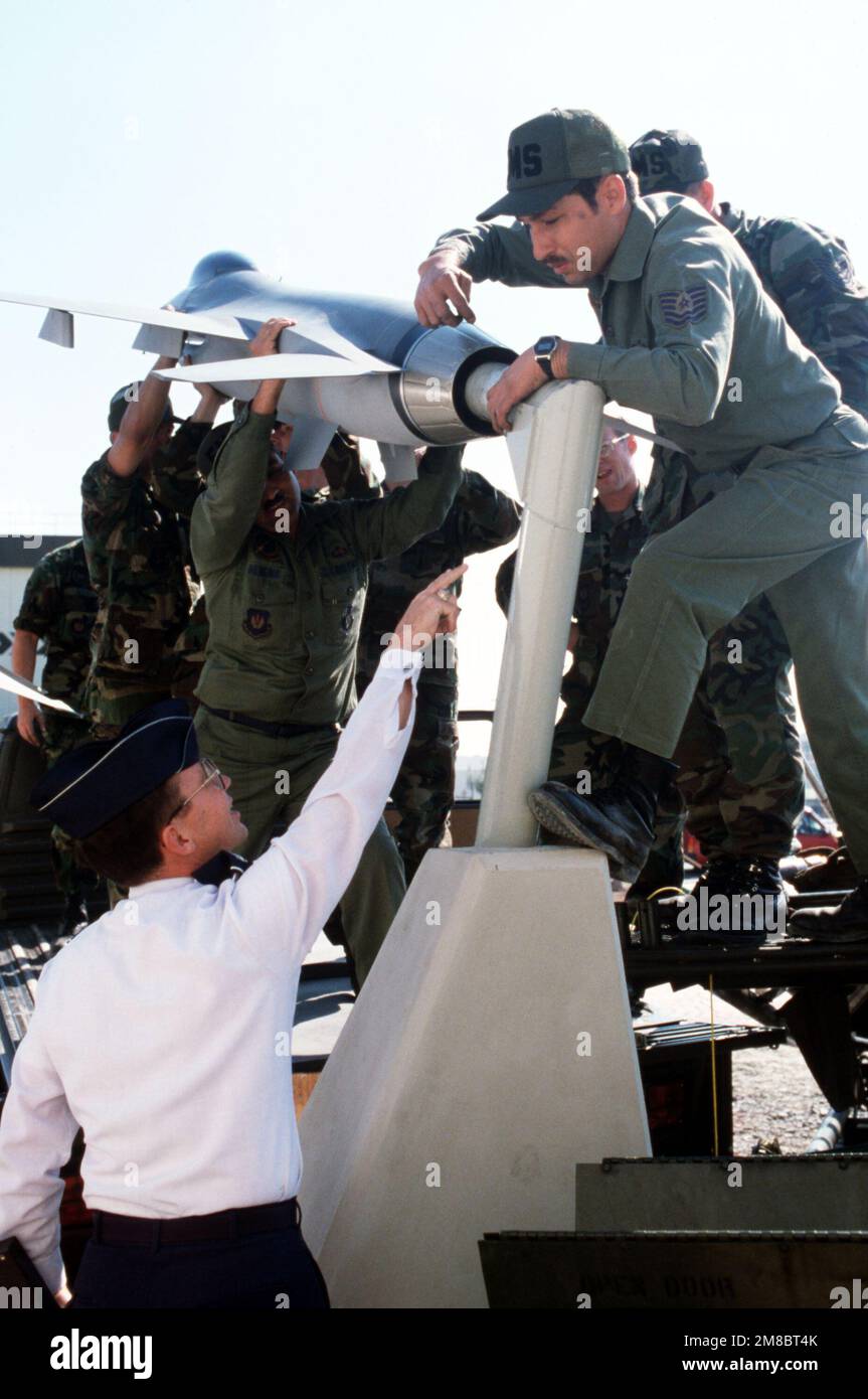 An officer directs a group of airmen who are attaching a model of an F ...