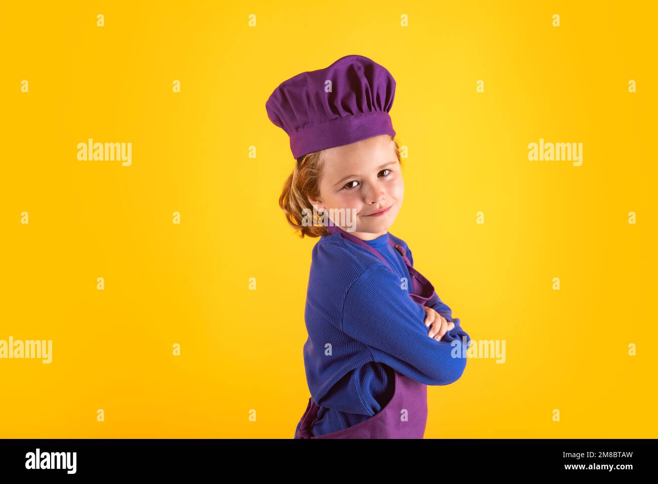 Kid in cooker uniform and chef hat preparing food on studio color ...