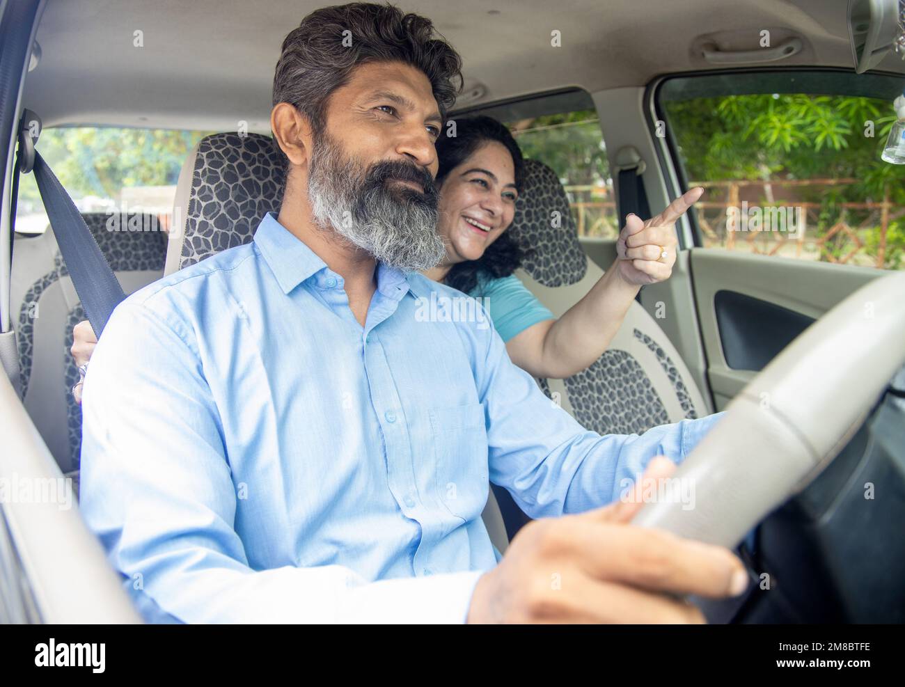 Mature indian man taxi driver driving cab with woman passenger pointing ...