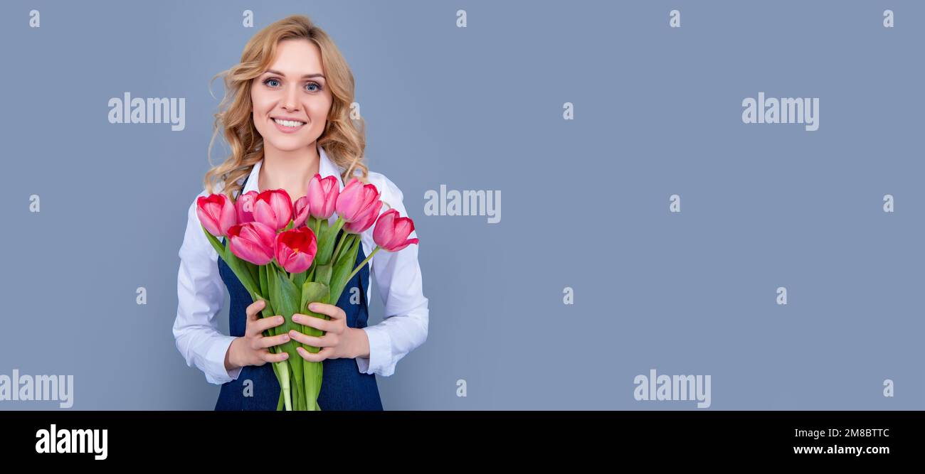 smiling young woman in apron with spring tulip flowers on grey ...