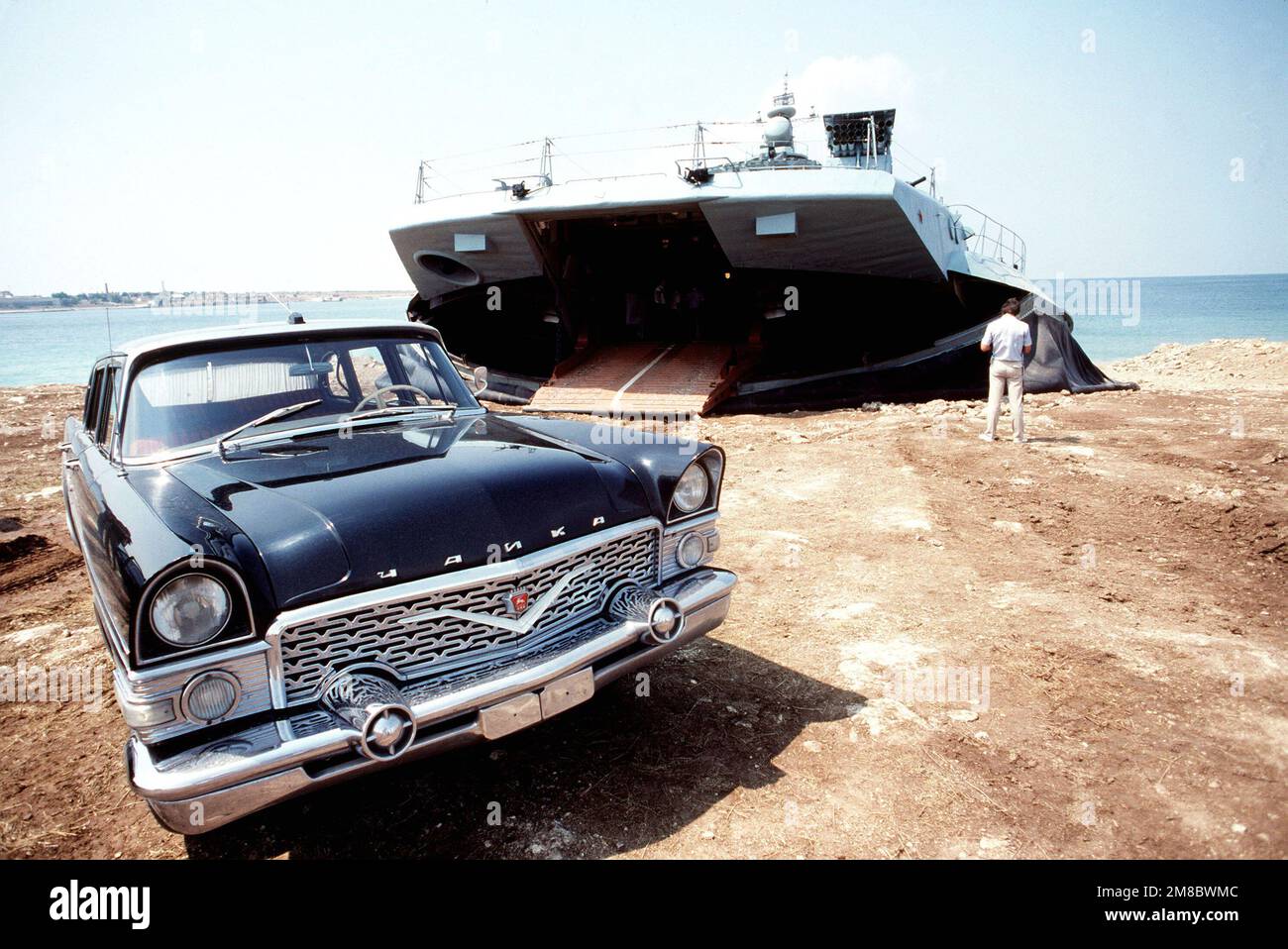 A Soviet Chaika automobile stands on the beach in front of a Pomornik ...