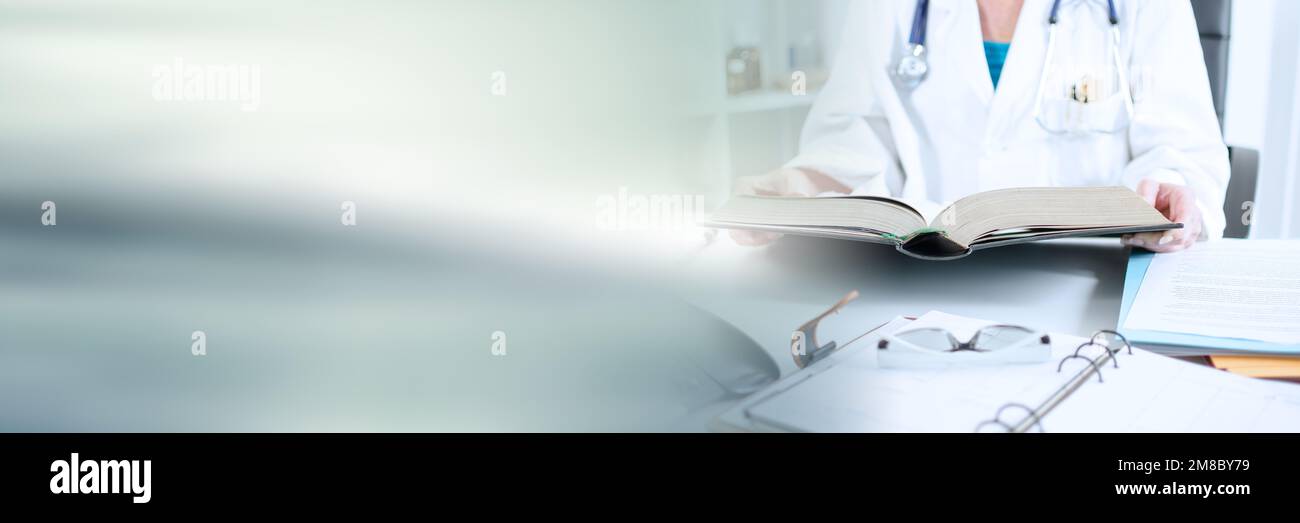 Female doctor reading a medical book at her desk; panoramic banner ...