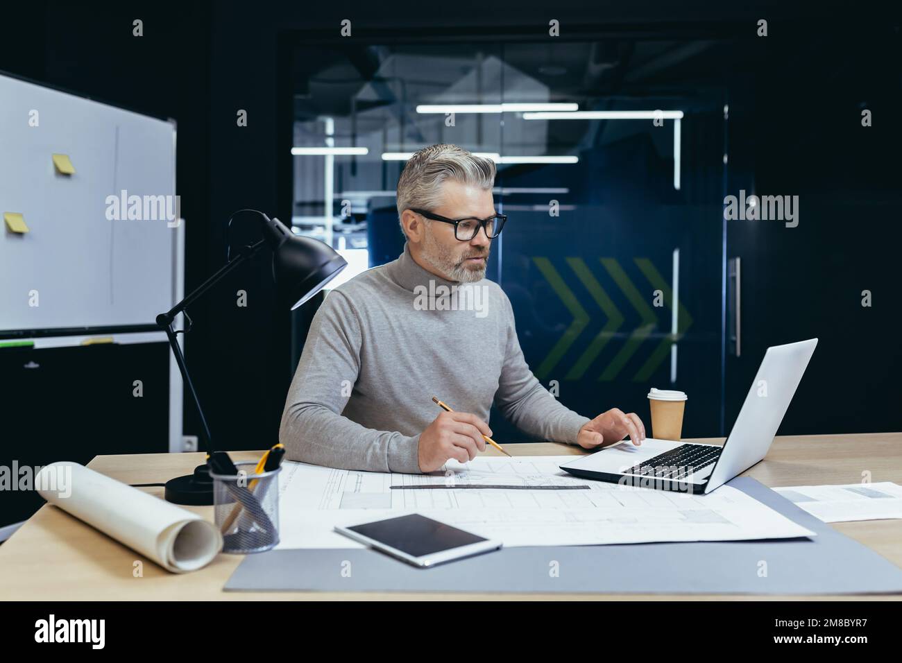 Senior gray-haired man architect, engineer, designer sits in the office ...