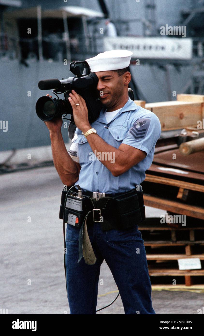 A photographer's mate uses a video camera to film supply loading aboard ...