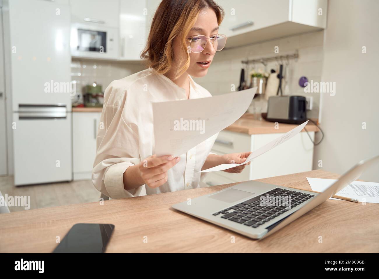 Concentrated lady with papers sitting at portable computer Stock Photo ...