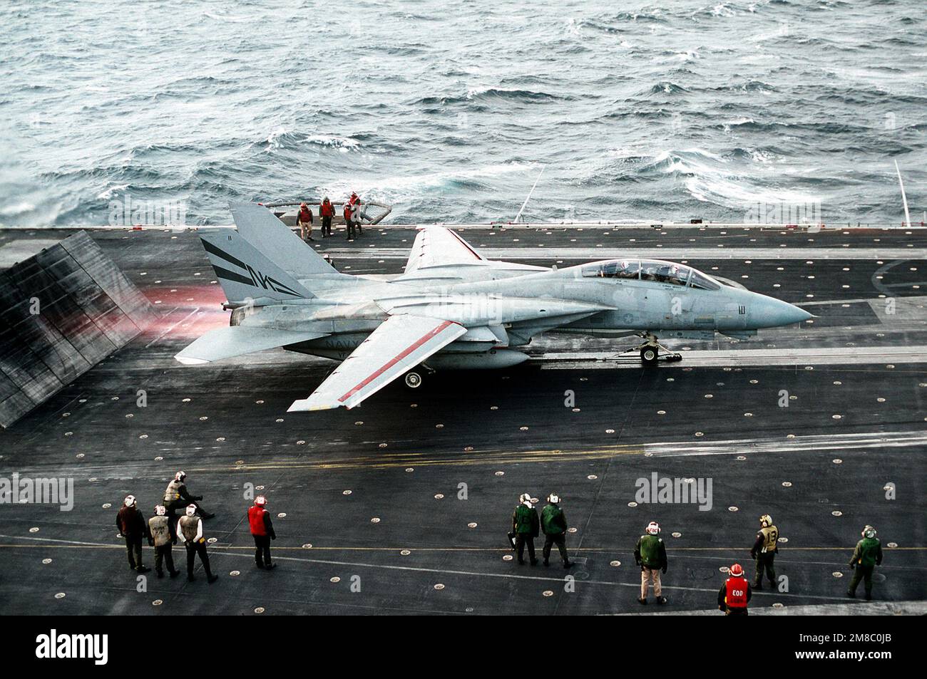 Flight deck crewmen watch as an F-14A Tomcat aircraft of Fighter ...