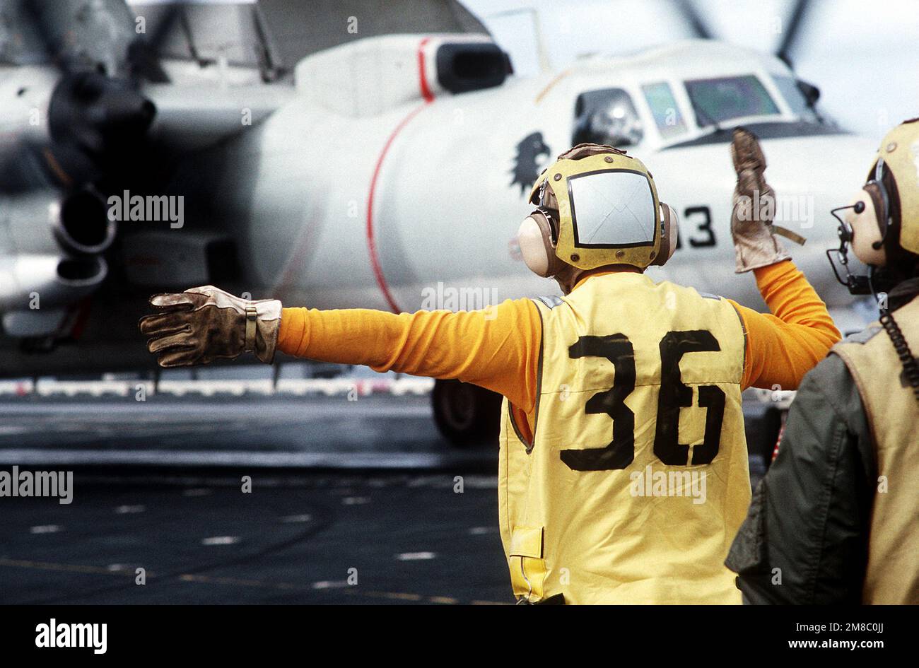 A plane director signals to the pilot of an E-2C Hawkeye aircraft as ...