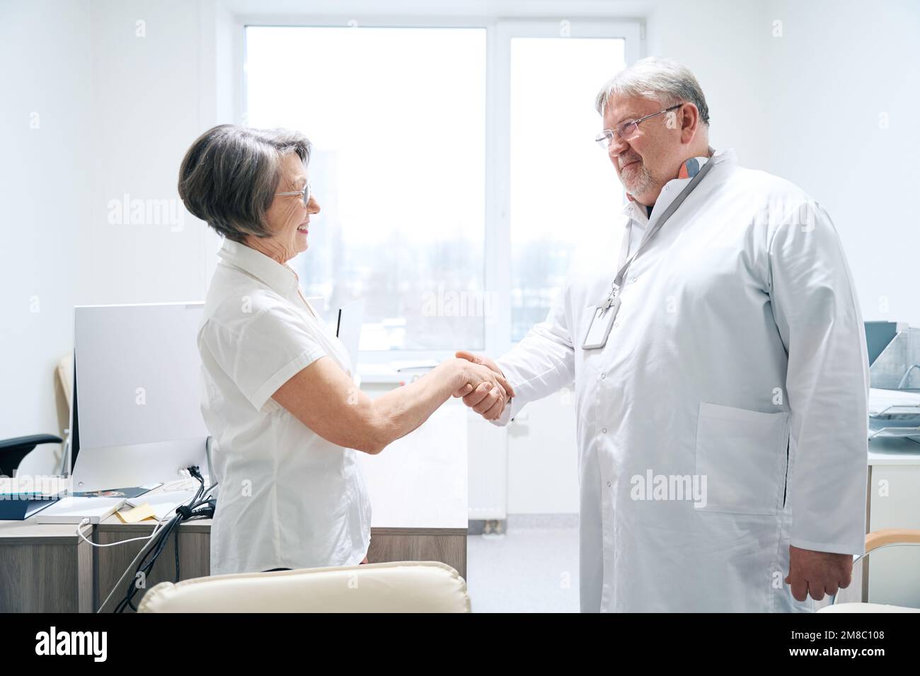 Friendly doctor greets with handshake elderly woman in medical office ...