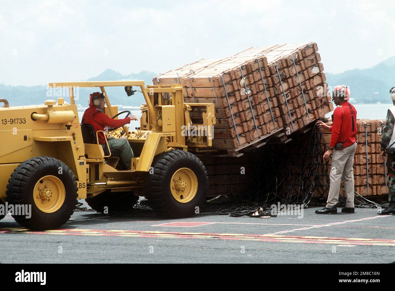 A sailor driving a forklift stacks a pallet of ammunition crates on a ...