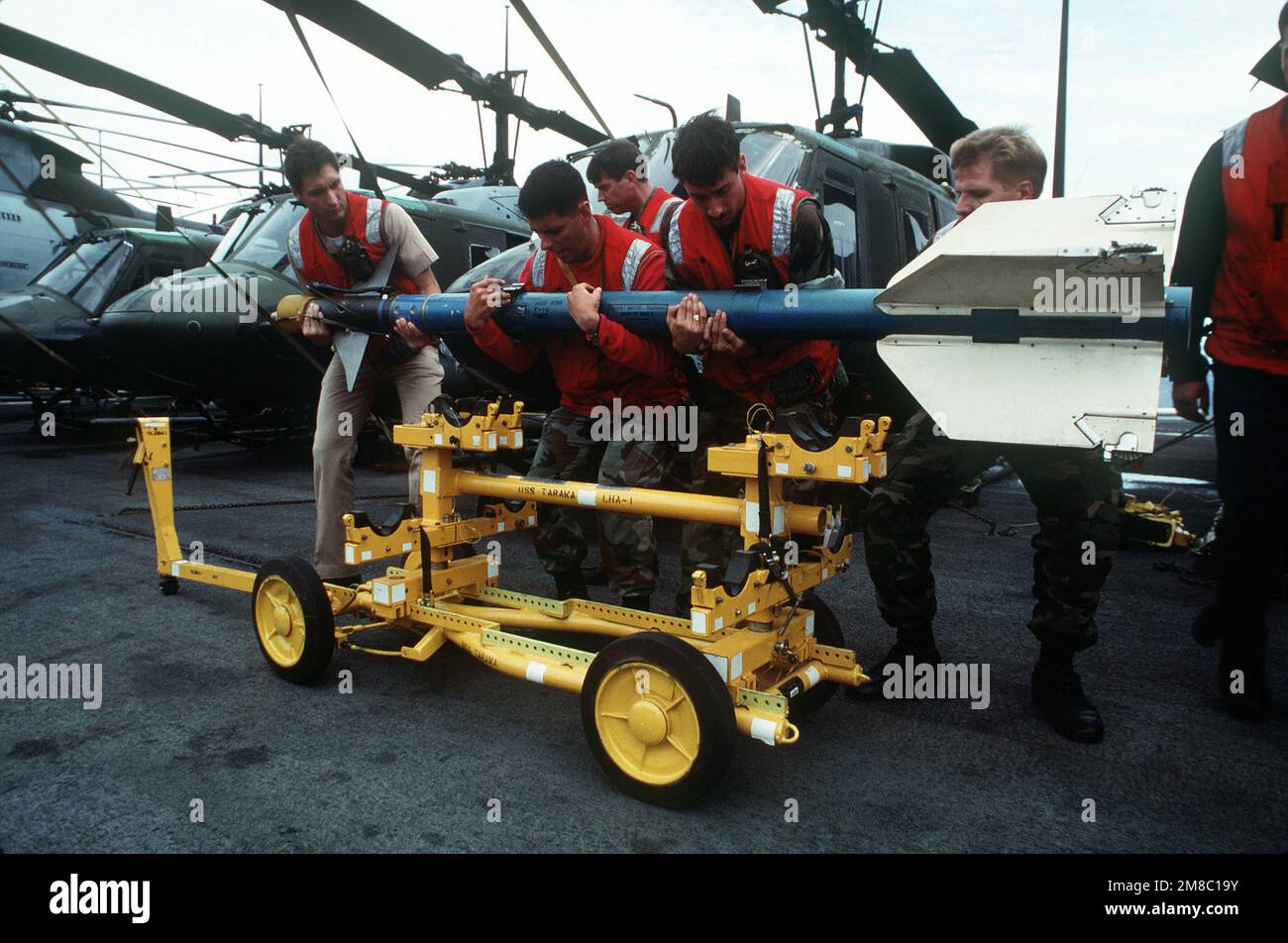 A Navy officer helps Marine ordnancemen lift an AIM-9 Sidewinder ...