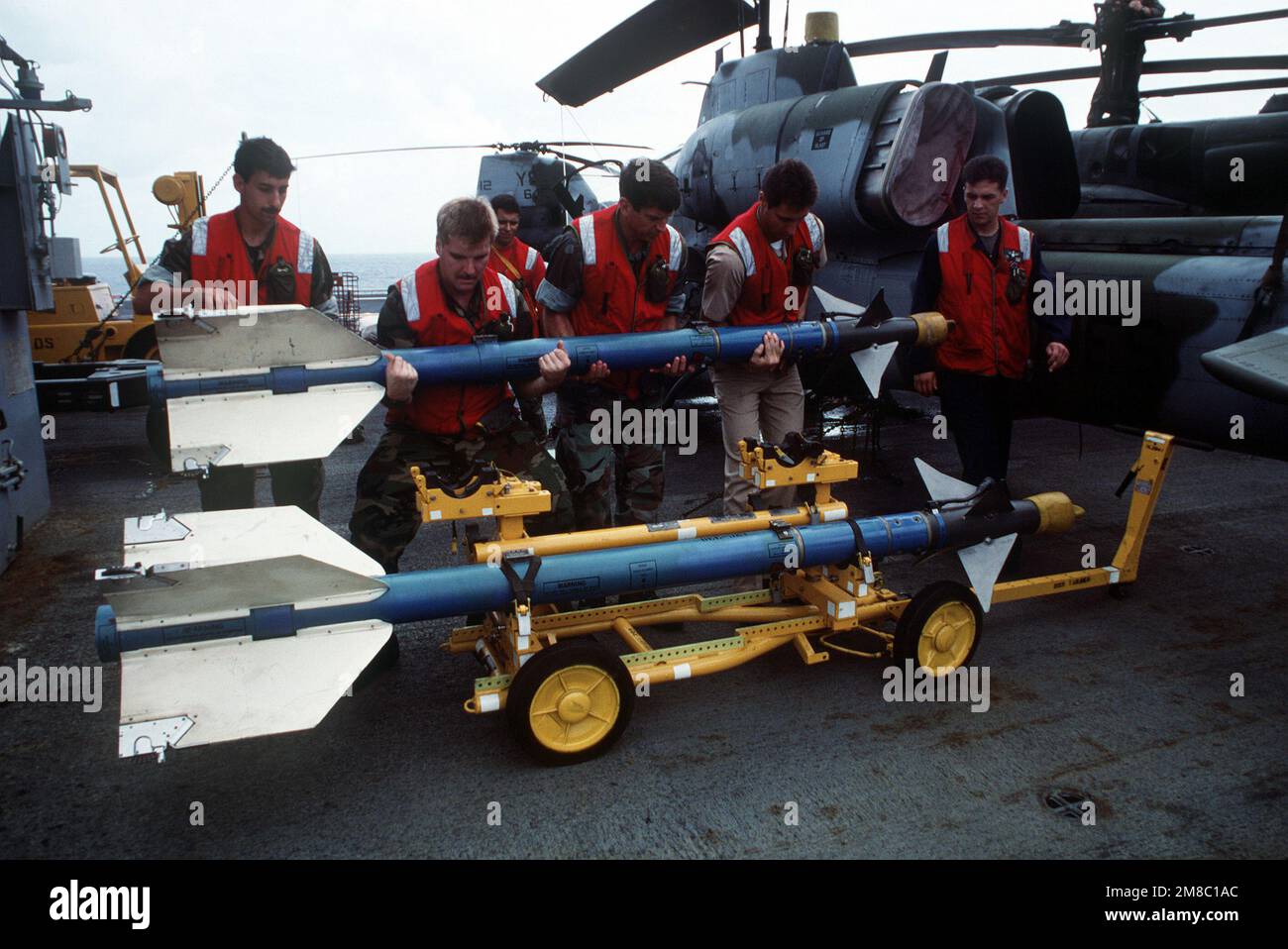 A Navy officer helps Marine ordnancemen lift an AIM-9 Sidewinder ...
