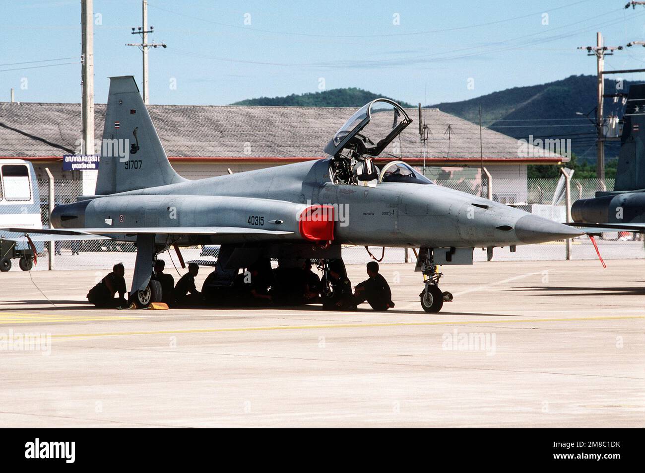 Thai ground crewmen sit in the shade beneath a Royal Thai Air Force F-5E Tiger II aircraft ...