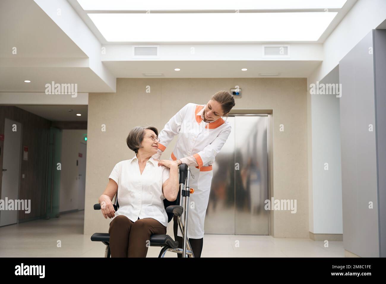 Medical worker is carrying patient in a wheelchair through foyer Stock ...