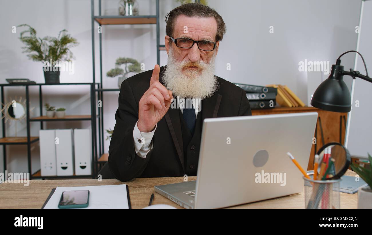 Senior old businessman working on laptop computer shakes finger and ...