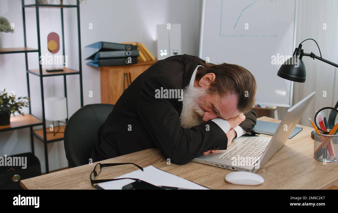 Bored sleepy old businessman worker working on laptop computer, yawning ...