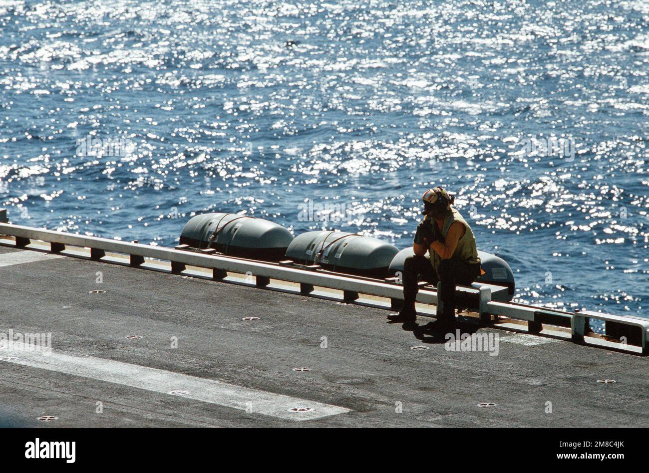 A flight deck crewman sits on the deck of the amphibious transport dock ...