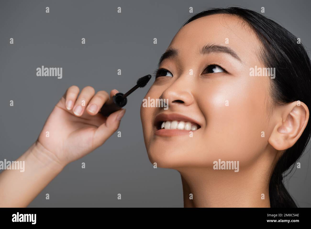 portrait of young asian woman with perfect smile applying black mascara ...