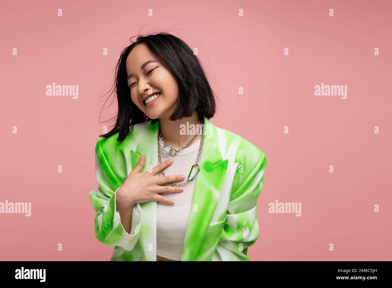excited and trendy asian woman holding hand on chest while laughing ...