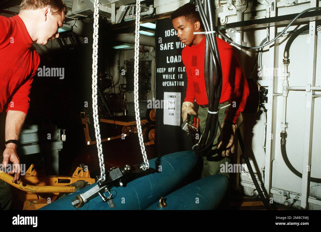 An ordnanceman uses an electrical hoist to maneuver a BDU-45 practice ...