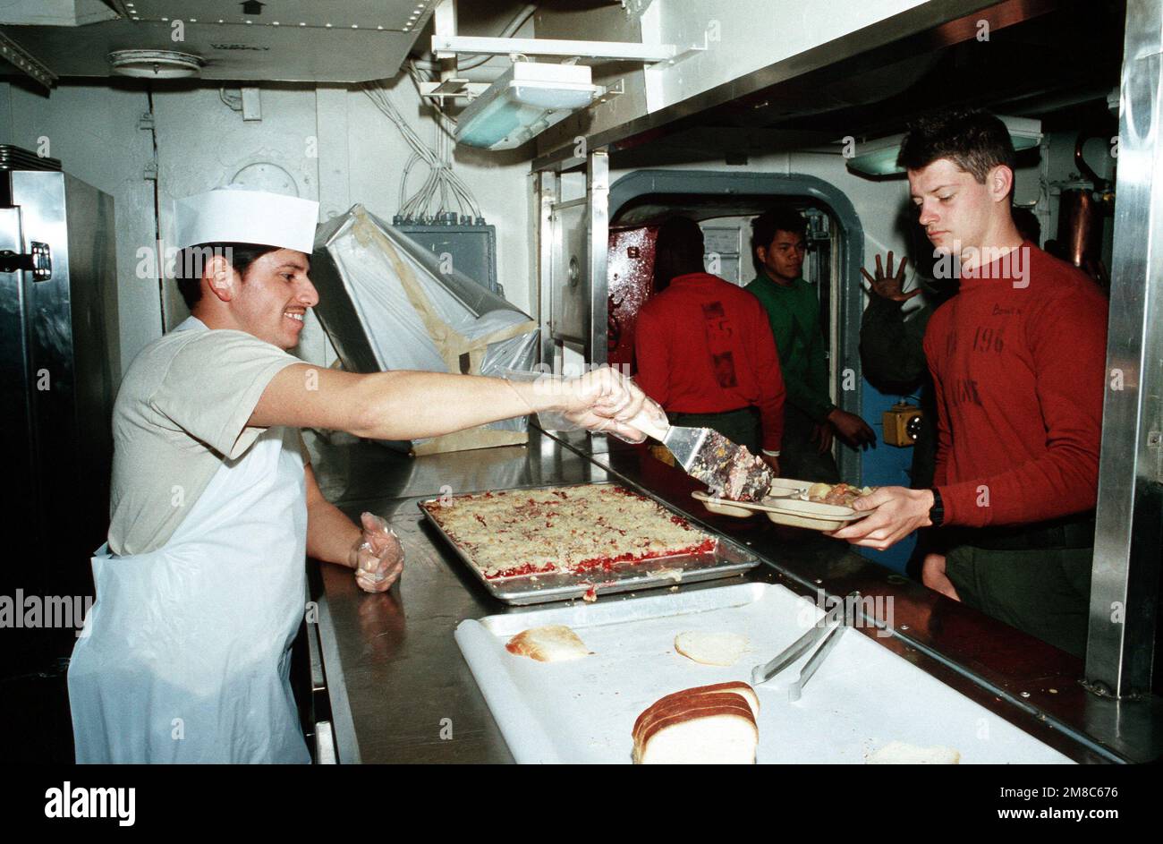 A mess management specialist serves dessert in the galley aboard the ...