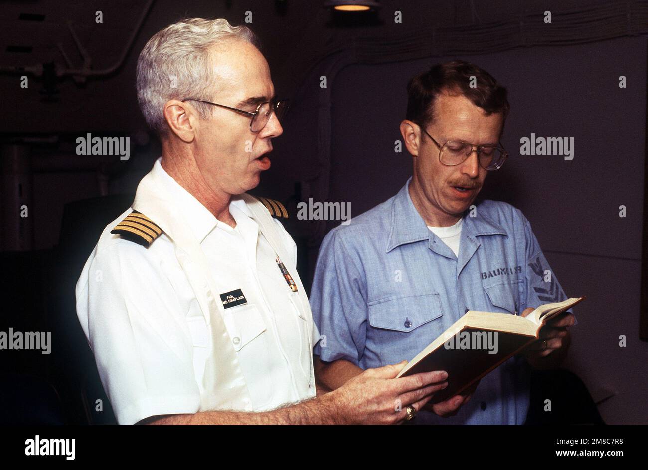 Chaplain (CPT) John R. Fiol joins a crew member in singing a hymn in ...