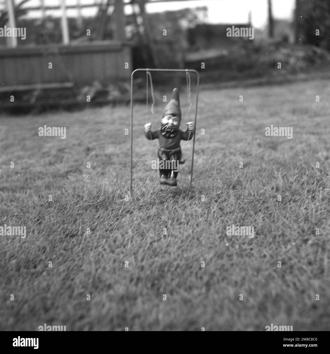 1950s, historical, a little garden gnome on swing sat on a grass lawn ...