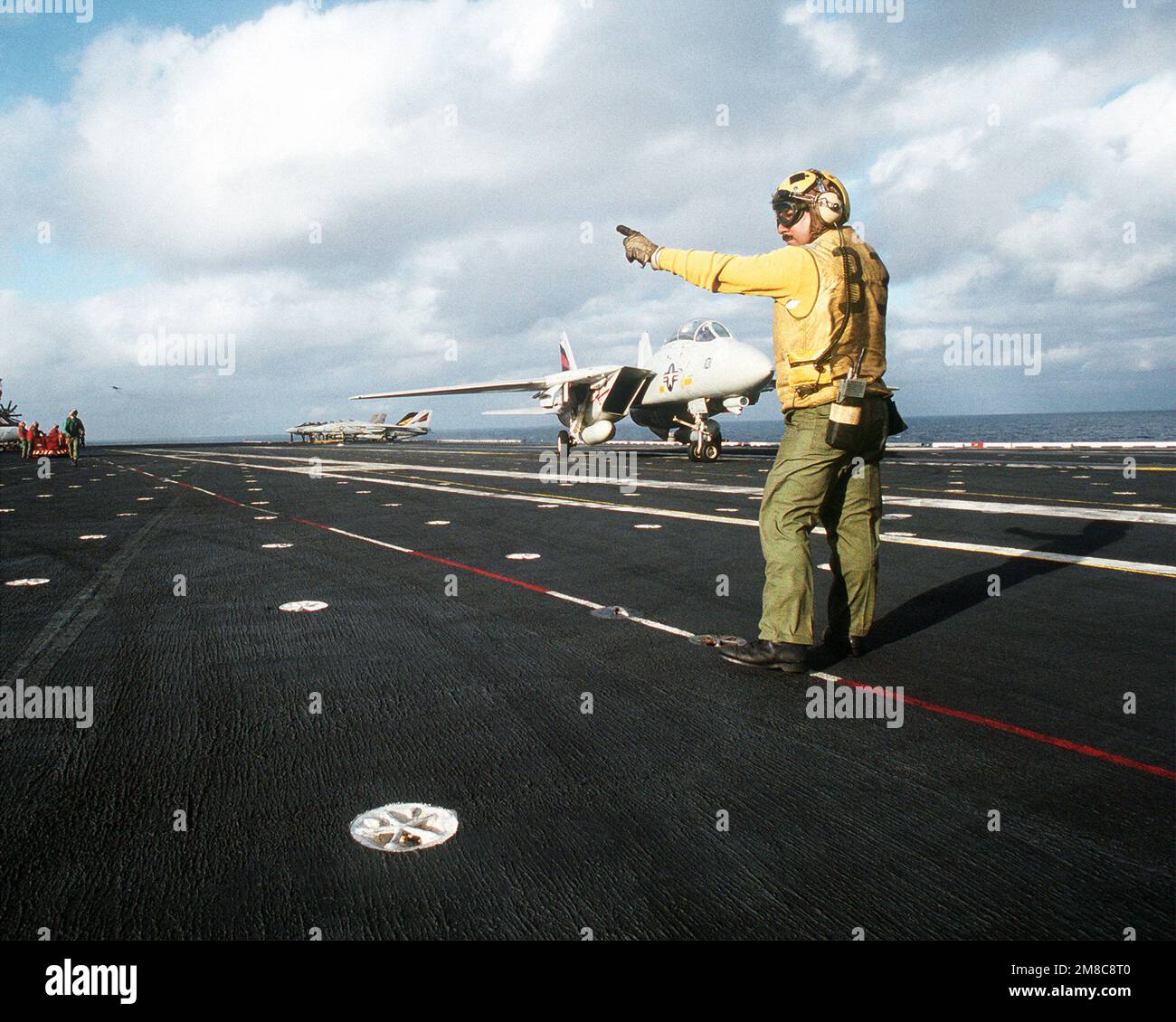 A flight deck crew member signals as an F-14A Tomcat aircraft on the ...
