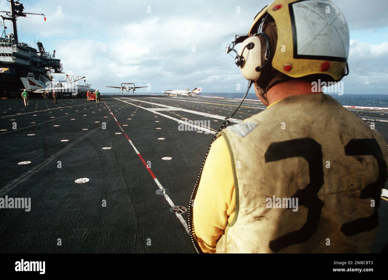 A flight deck crew member watches as an E-2C Hawkeye aircraft comes in ...