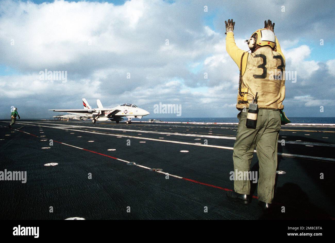A flight deck crew member signals to the pilot of an F-14A Tomcat ...
