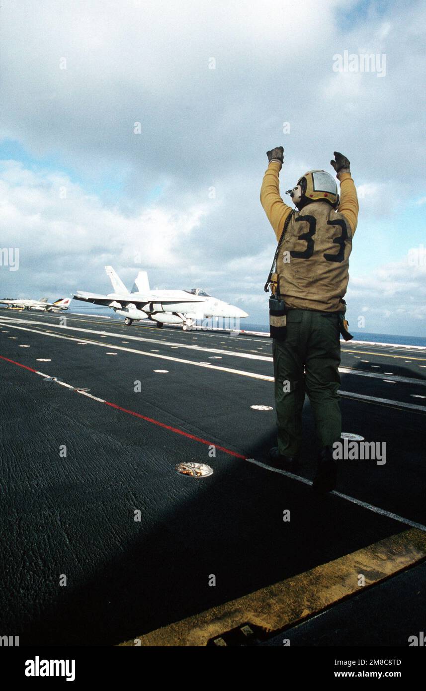 A flight deck crew member signals to the pilot of a Strike Fighter ...