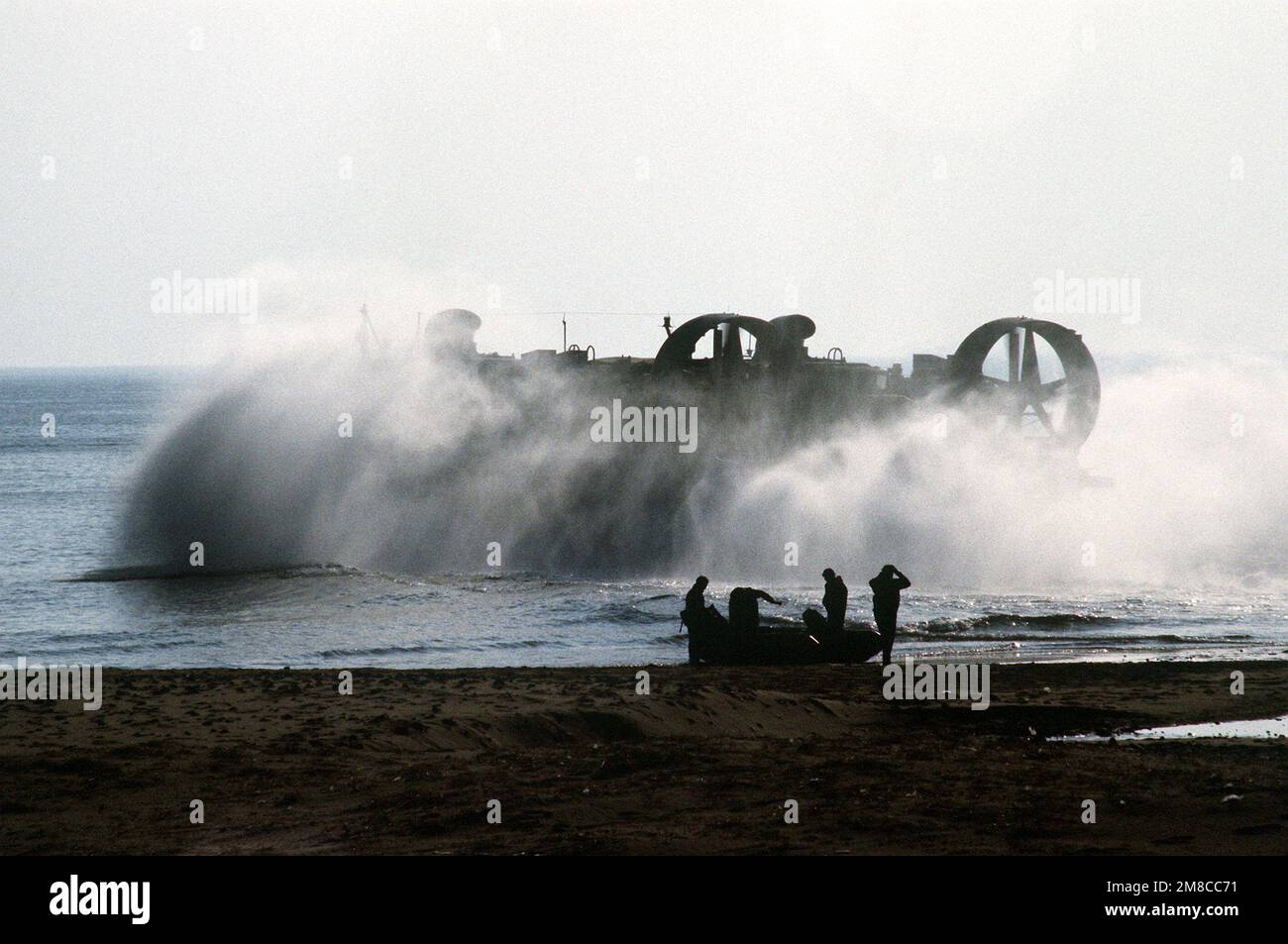 An air-cushion landing craft (LCAC) moves off the beach in front of a ...