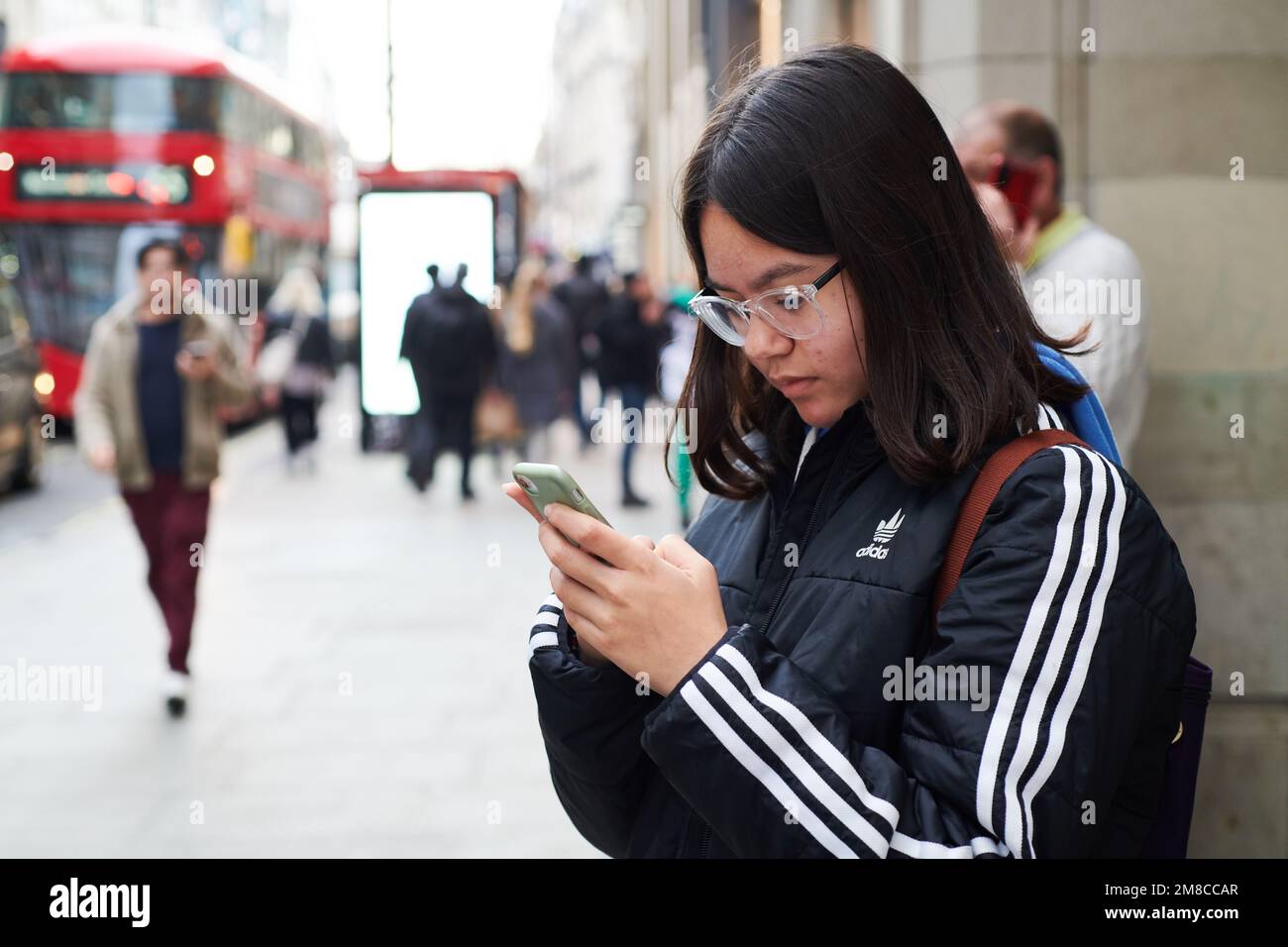 Teen girl checking her phone whilst standing outside in Oxford Street ...