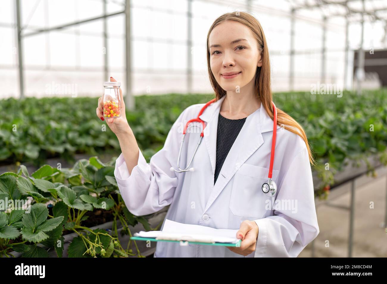 Doctor nutritionist in greenhouse farming proudly showing bottle of ...