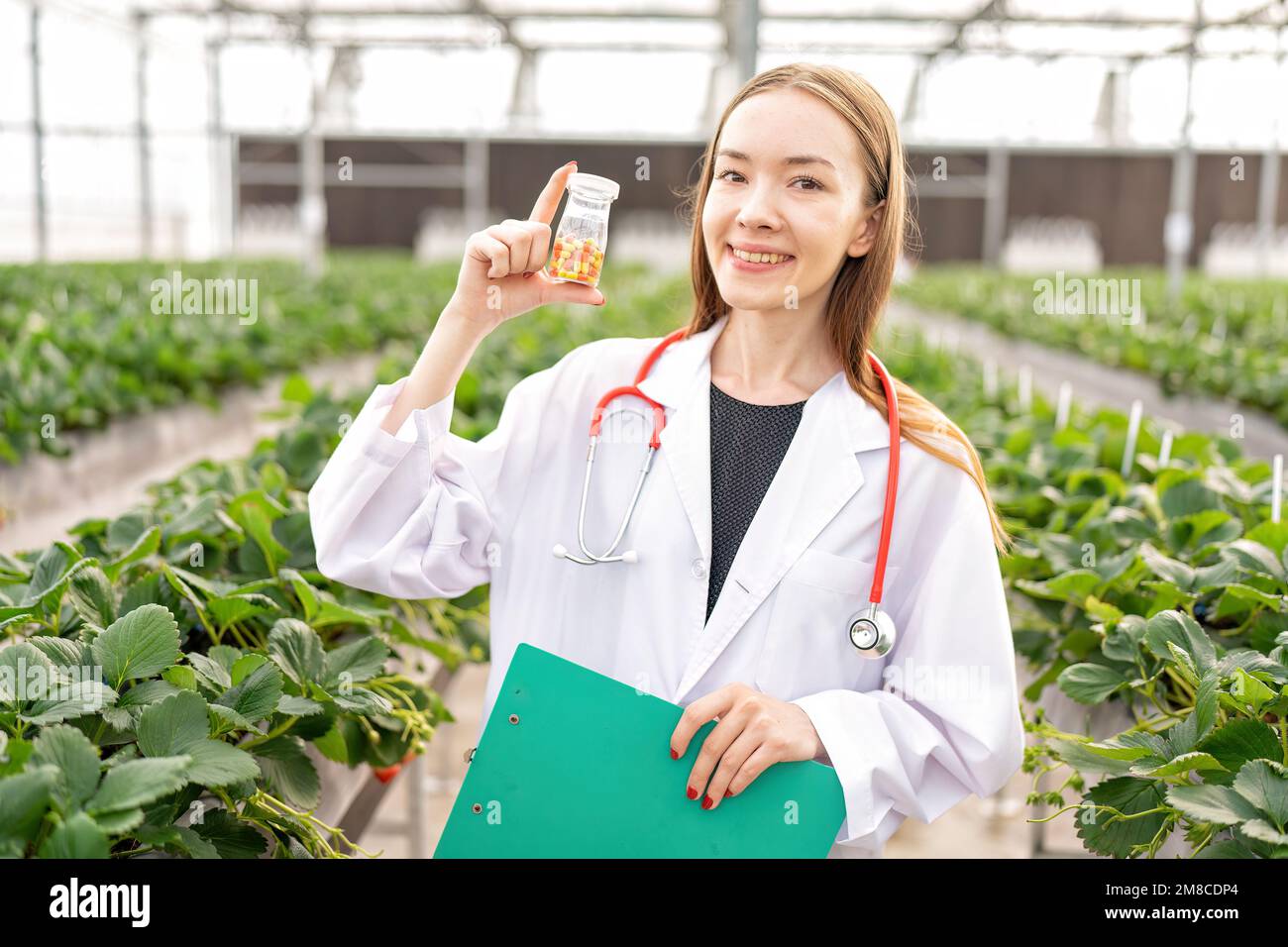 Doctor nutritionist in greenhouse farming proudly showing bottle of ...