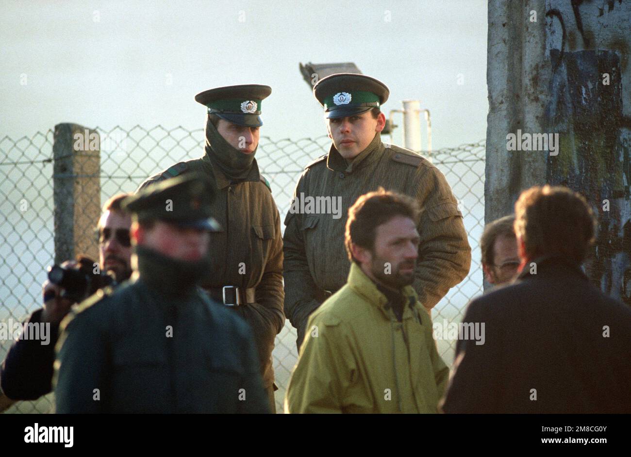 East German policemen watch visitors wander through a newly created ...