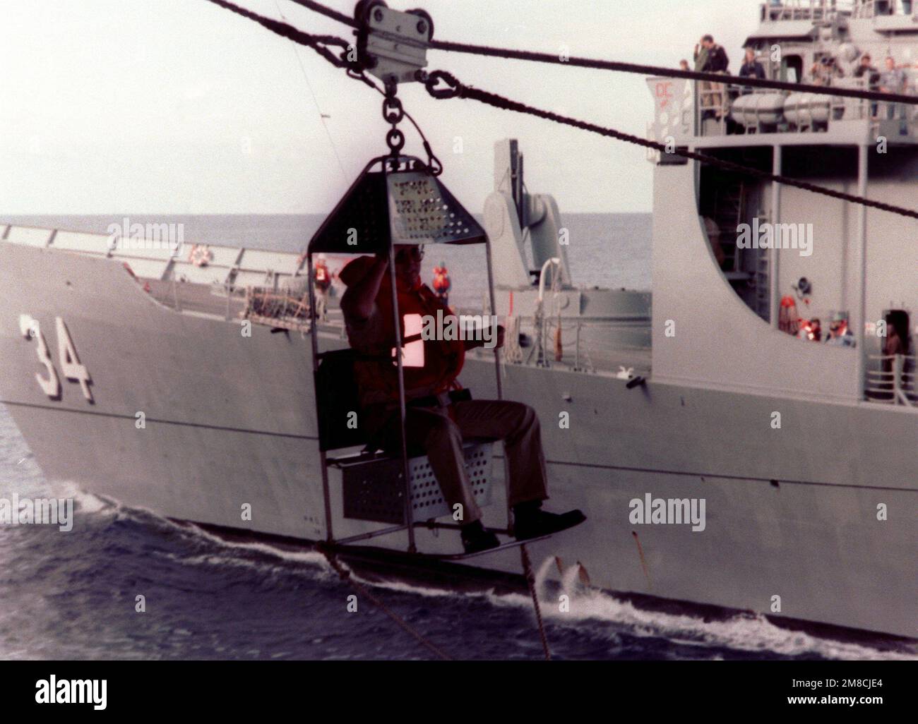 An officer in a transfer-at-sea chair on a manila highline rig travels ...