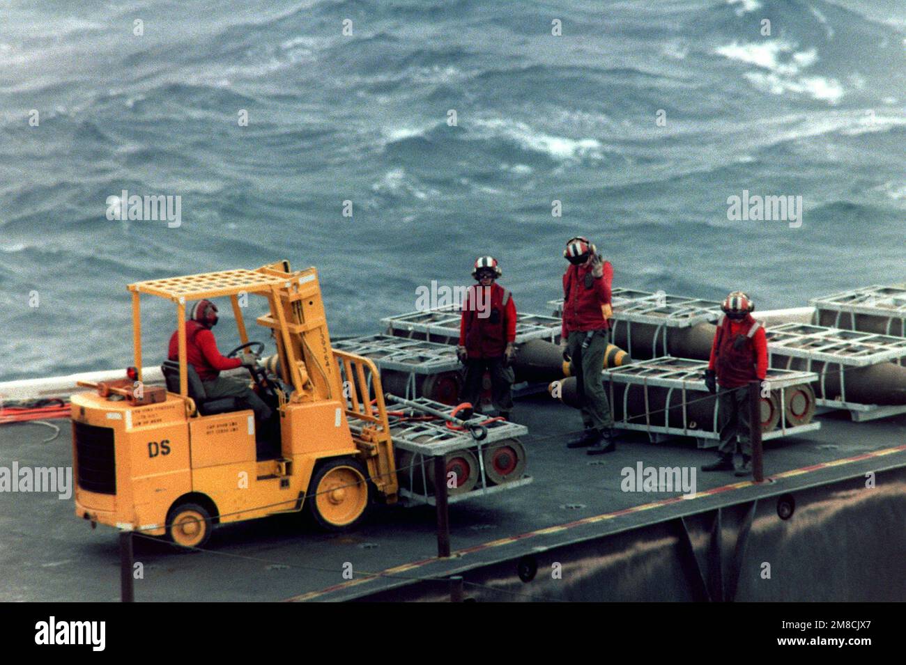 A flight deck crew member uses a forklift to move pallets of bombs ...