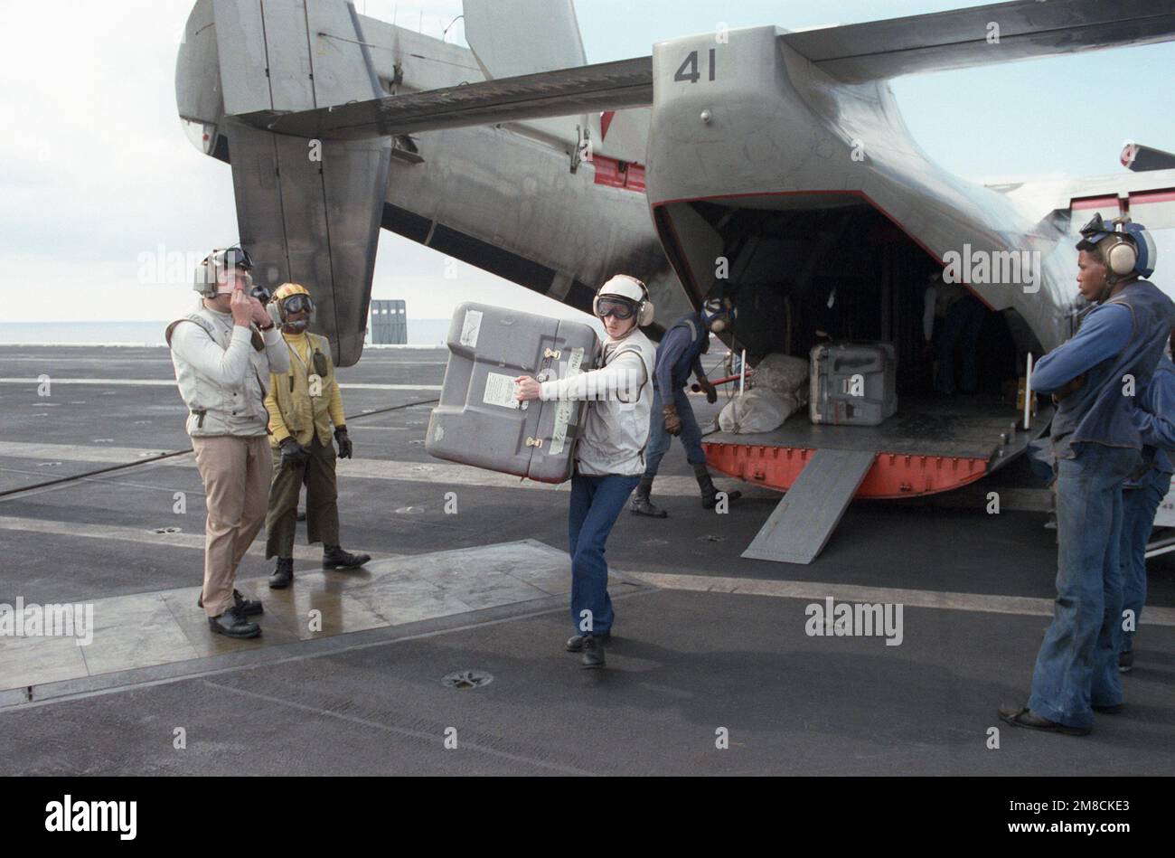 A sailor carries a box from the back of a C-2A Greyhound aircraft on ...