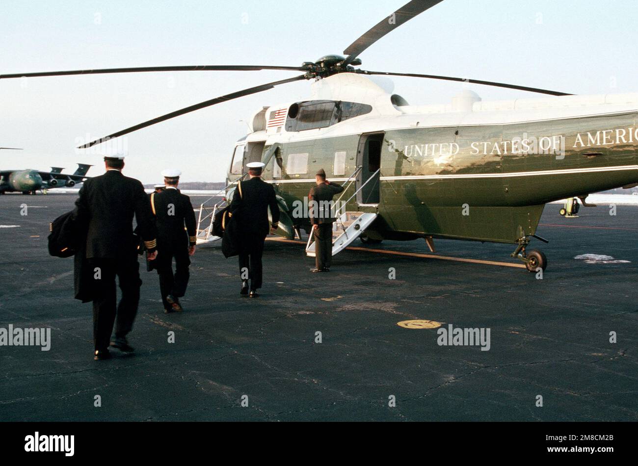 Navy officers cross the tarmac past a VH-3D Sea King helicopter from ...