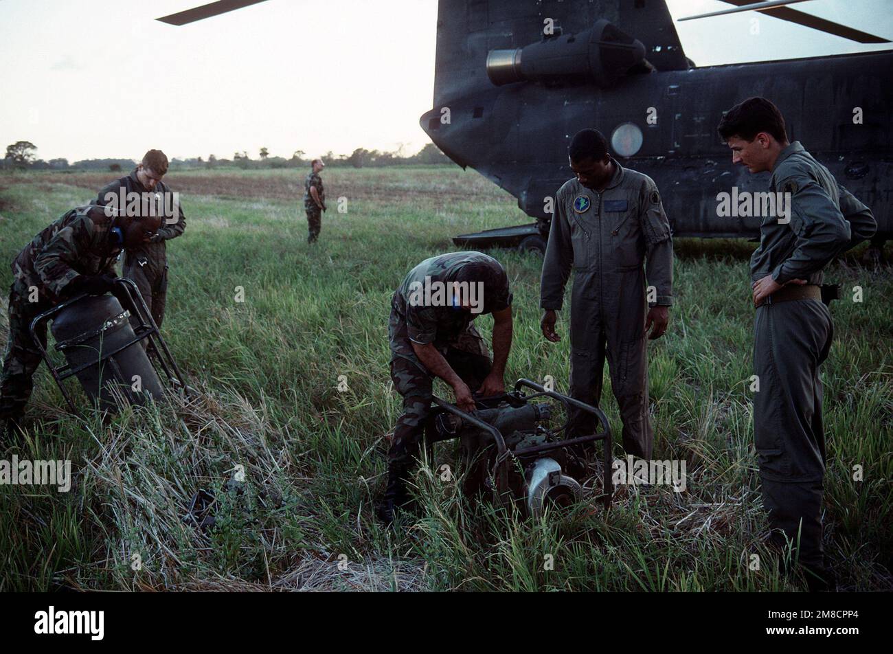 Soldiers set up refueling equipment in a field beside a CH-47 Chinook ...
