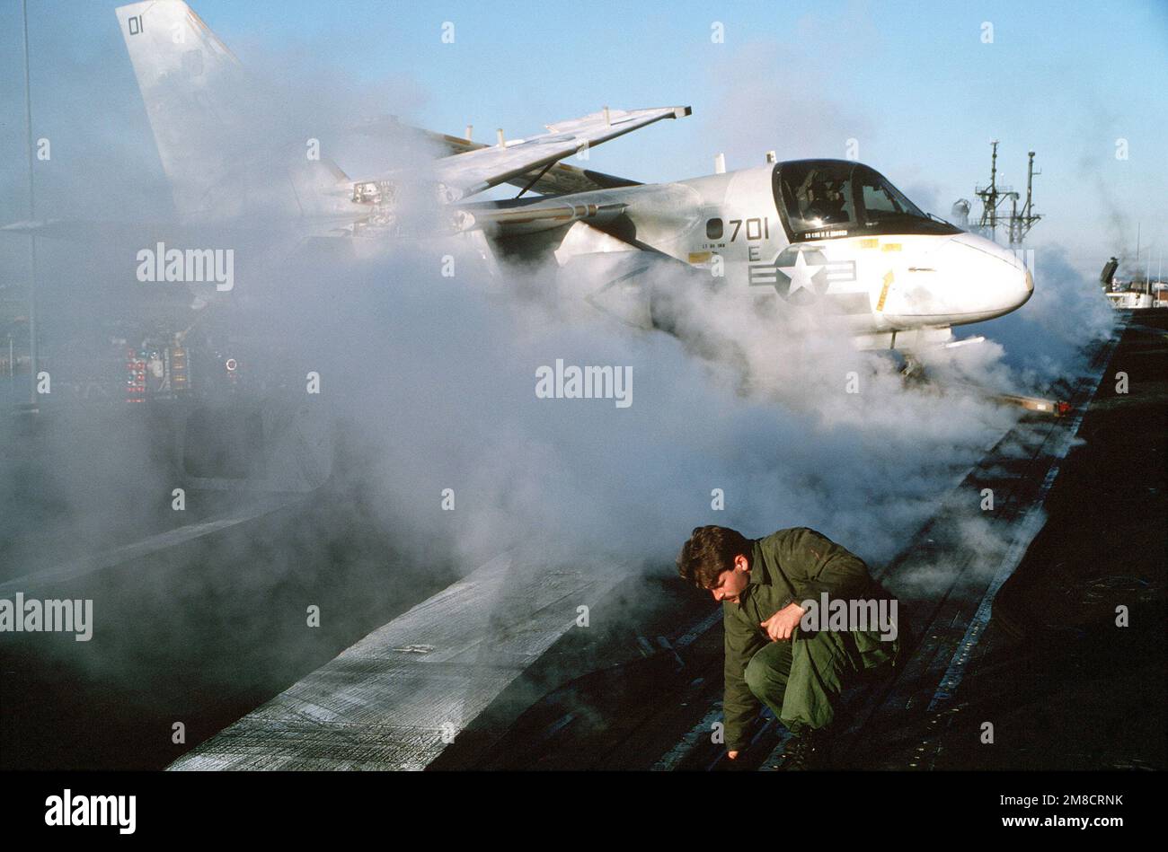 A flight deck crew member inspects a catapult as steam from the ...