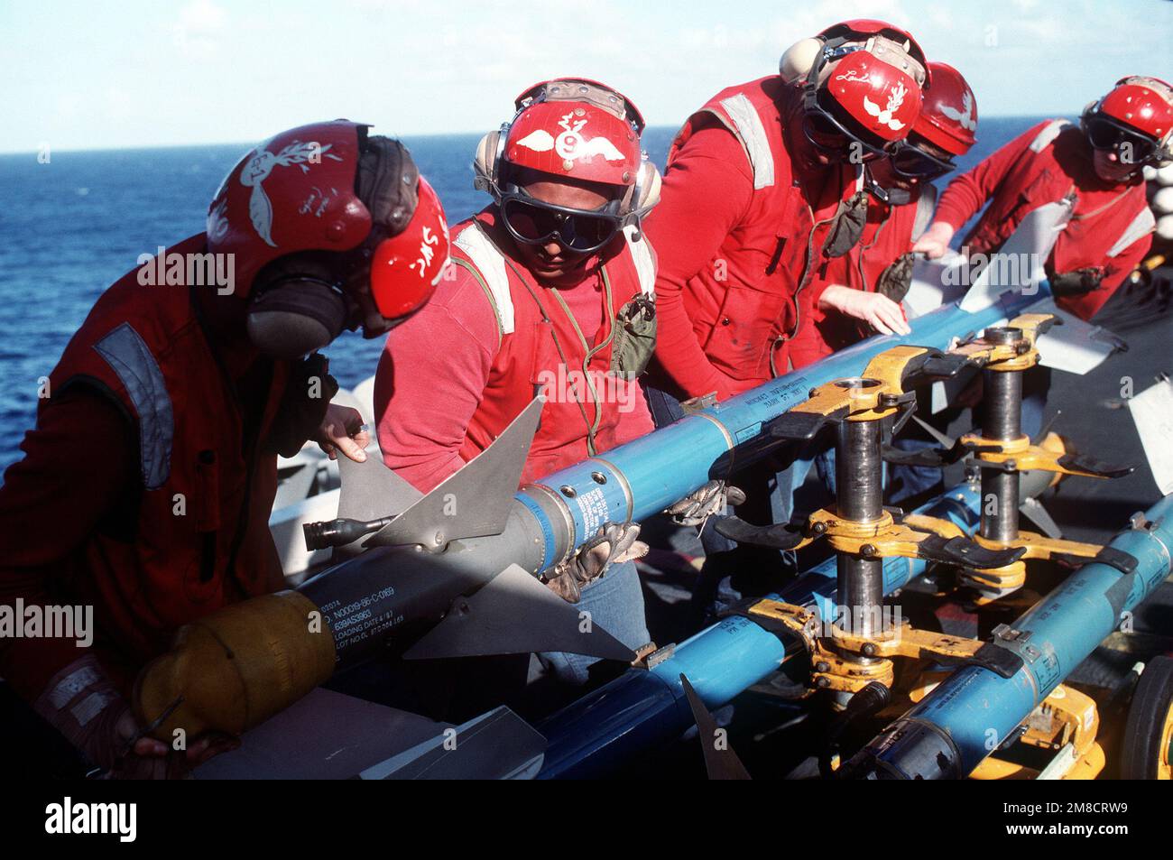 Ordnancemen lift an AIM-9 Sidewinder missile from a rack on the flight ...