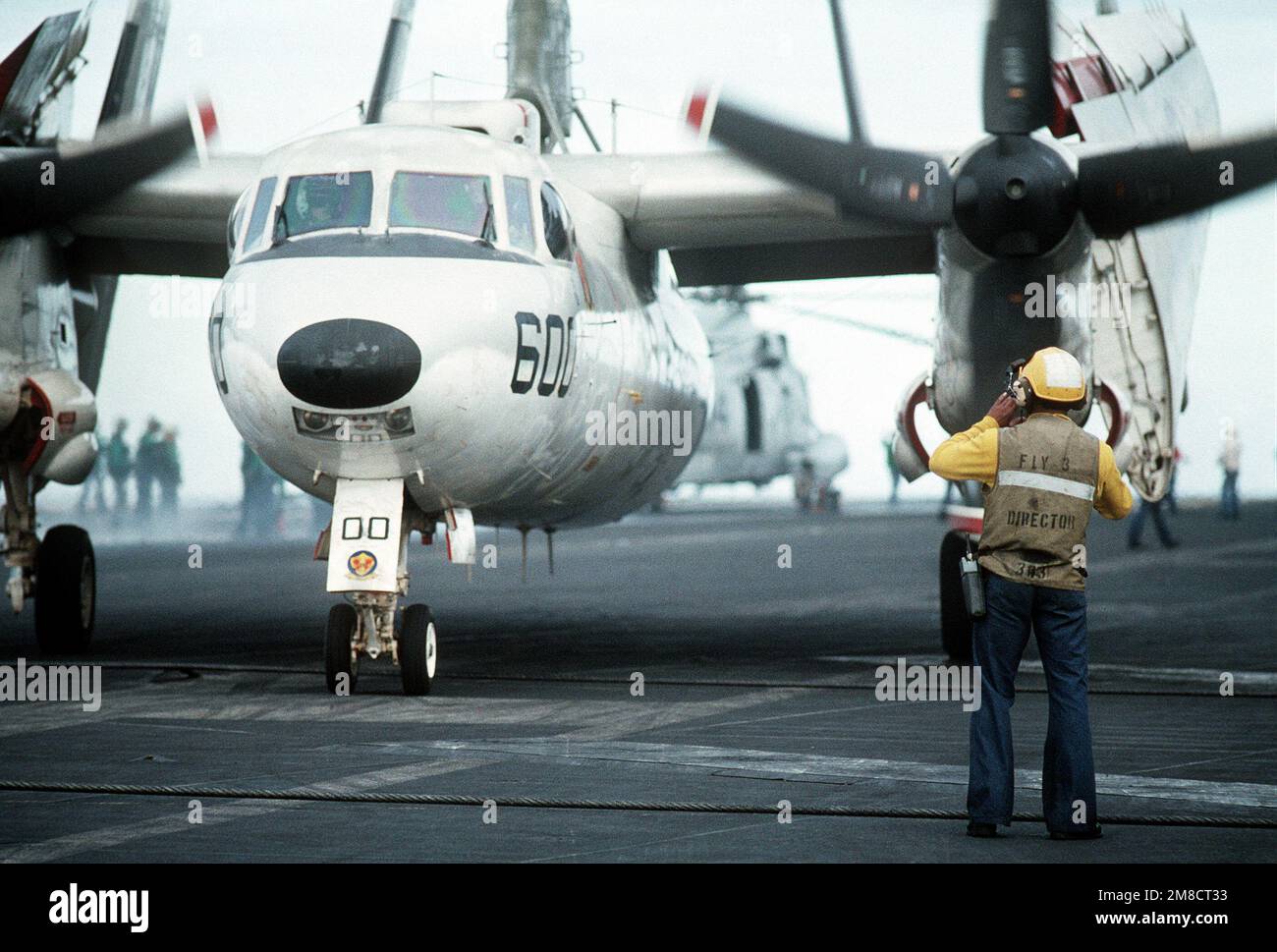 A plane director guides an E-2C Hawkeye aircraft on the flight deck of ...