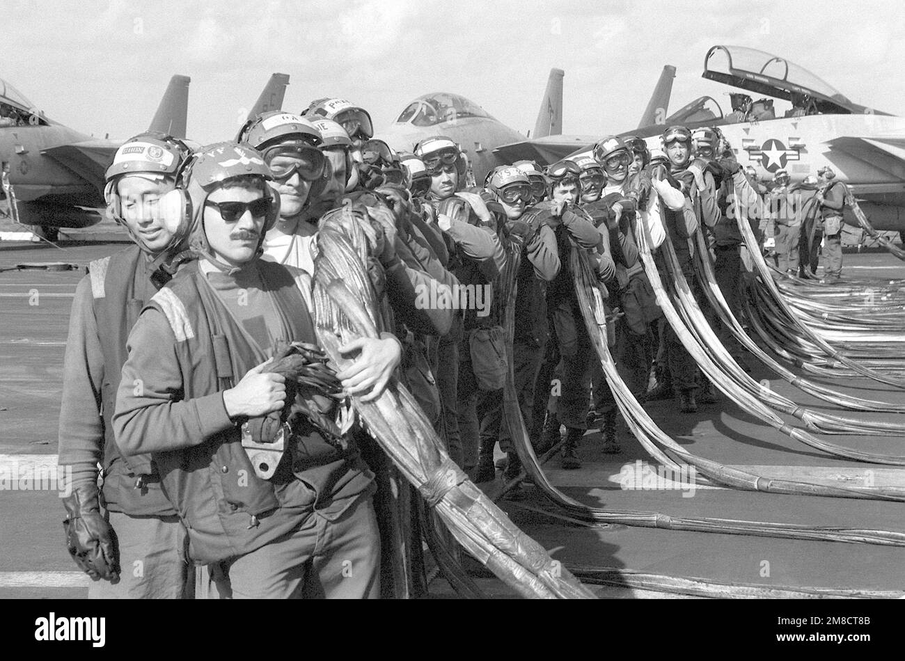 Flight deck crewmen carry the crash barricade back to its storage space ...