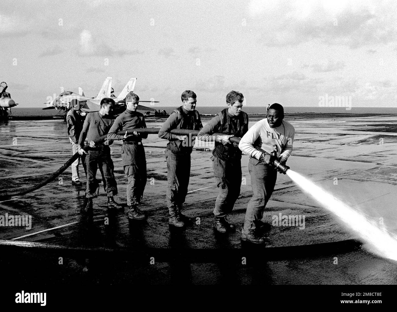 Sailors use a fire hose to rinse soap from the flight deck of the ...