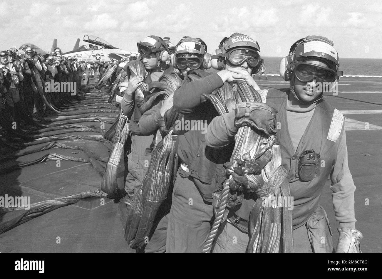 Flight deck crewmen carry the crash barricade back to its storage space ...