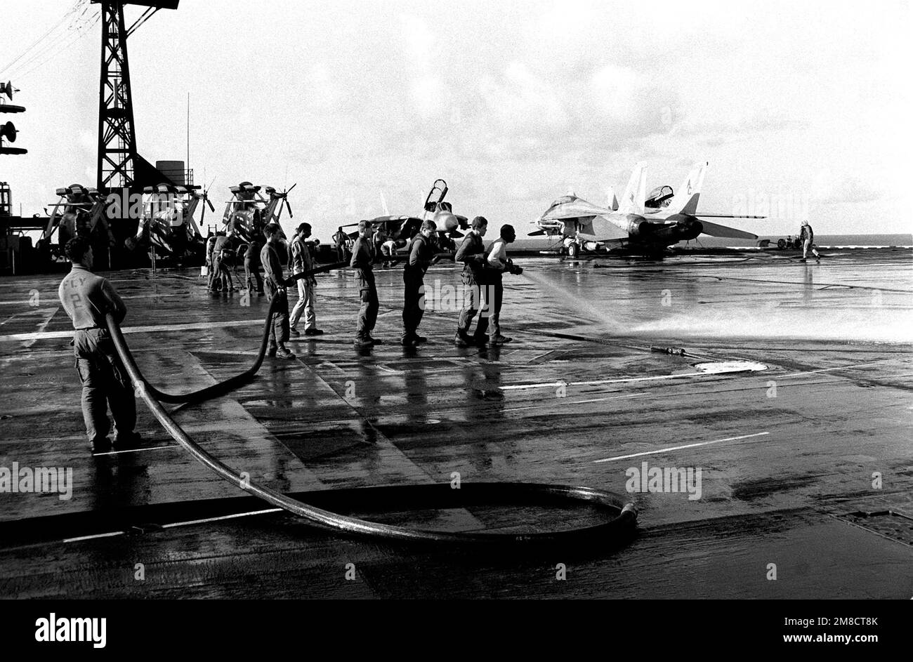 Sailors use a fire hose to rinse soap from the flight deck of the ...