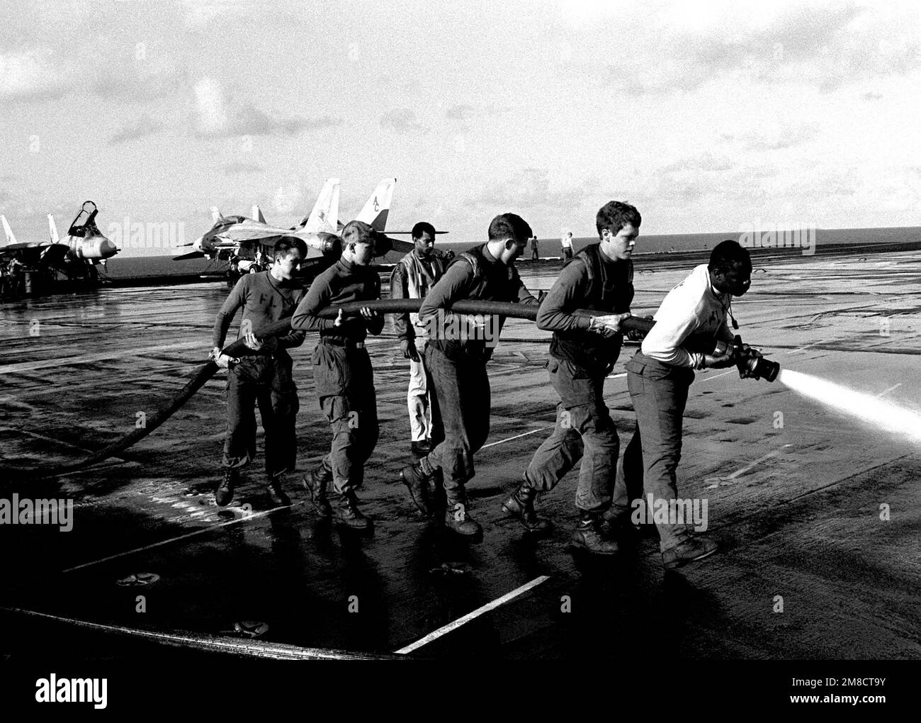 Sailors use a fire hose to rinse soap from the flight deck of the ...