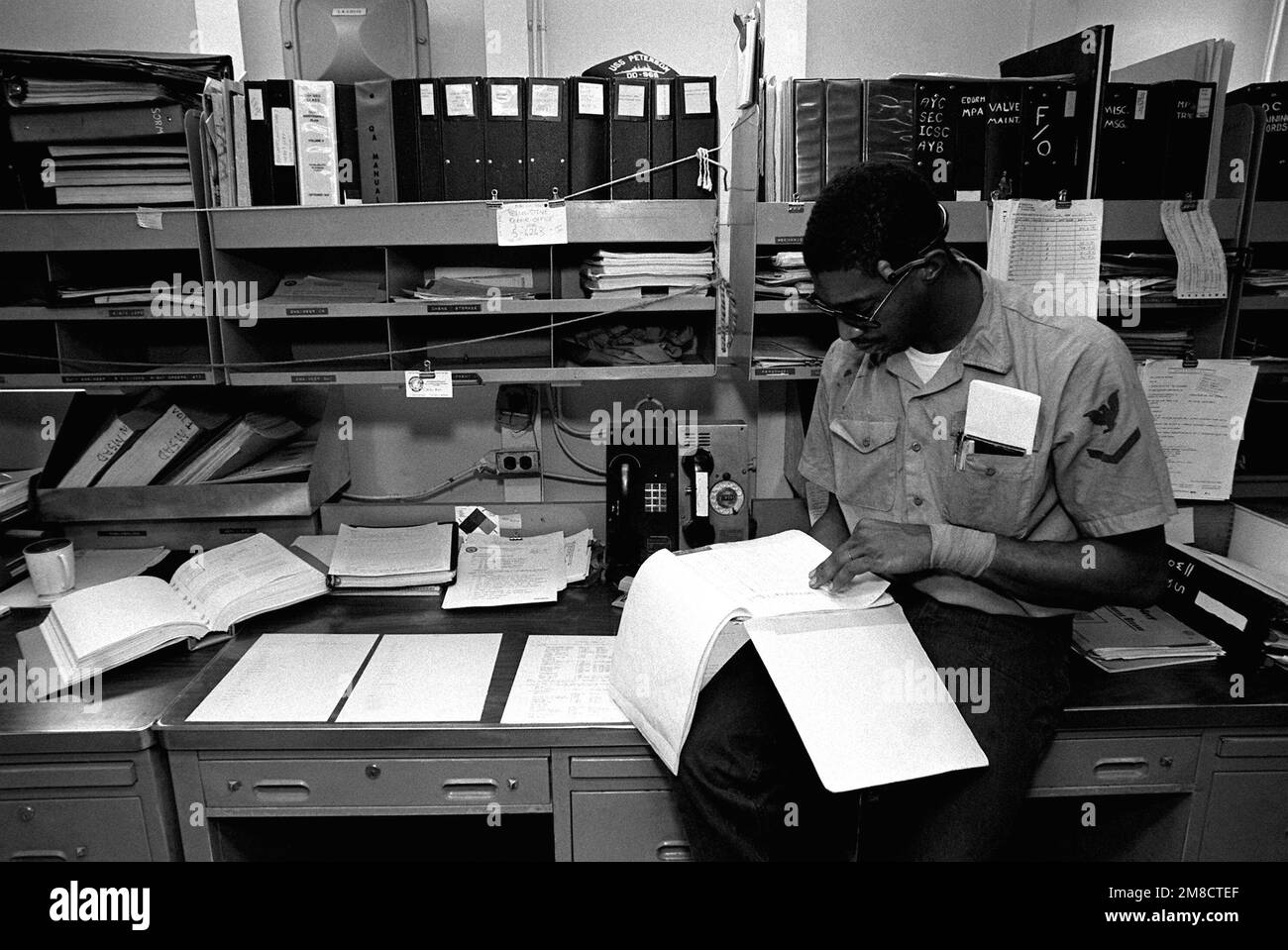 A petty officer checks supply records aboard the destroyer USS PETERSON ...